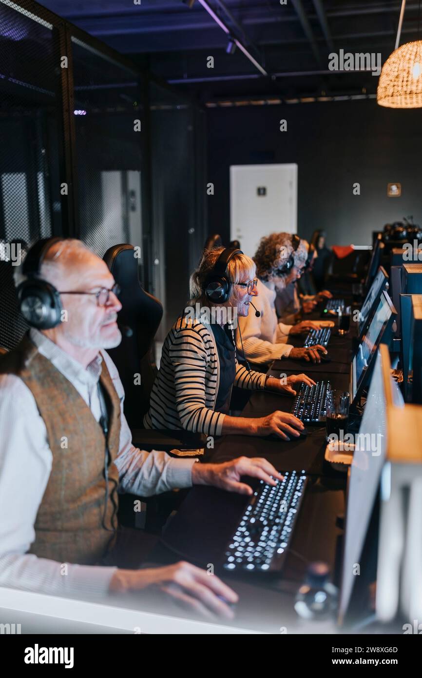 Senior male and female friends playing video game on computers in ...