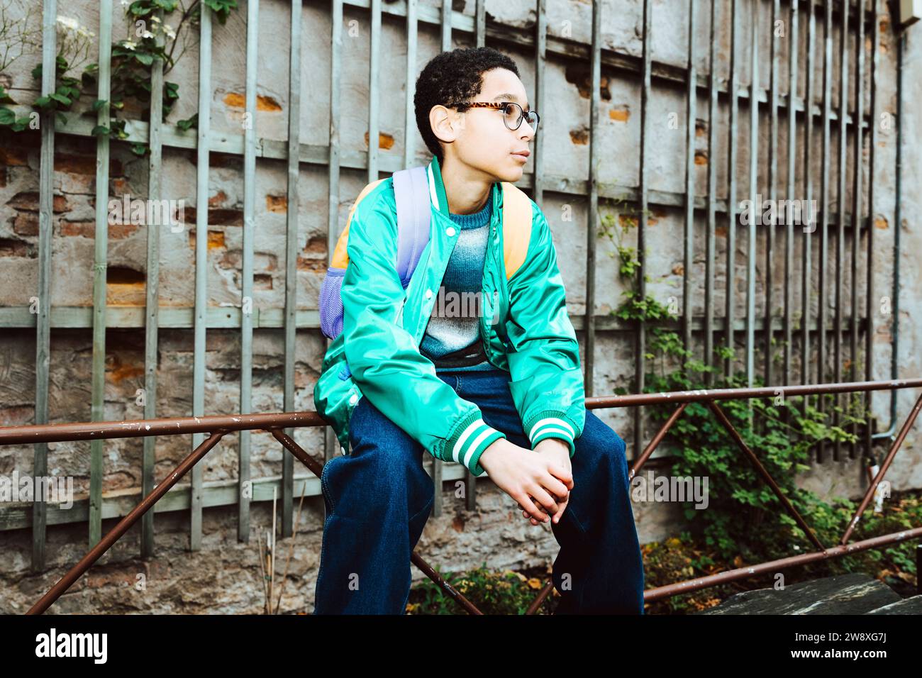 Contemplative boy looking away while sitting on railing Stock Photo - Alamy
