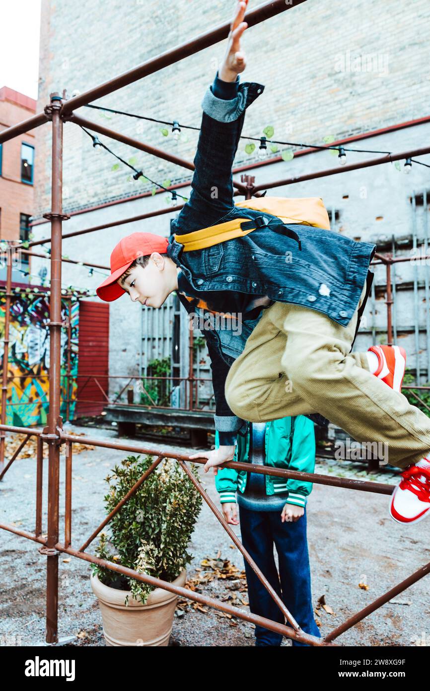 Boy jumping over railing by male friend standing on footpath during ...