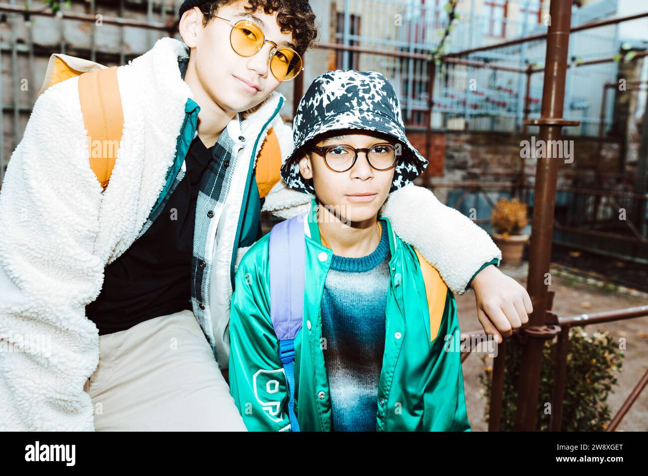 Portrait of boy arm around with male friend while sitting on railing ...