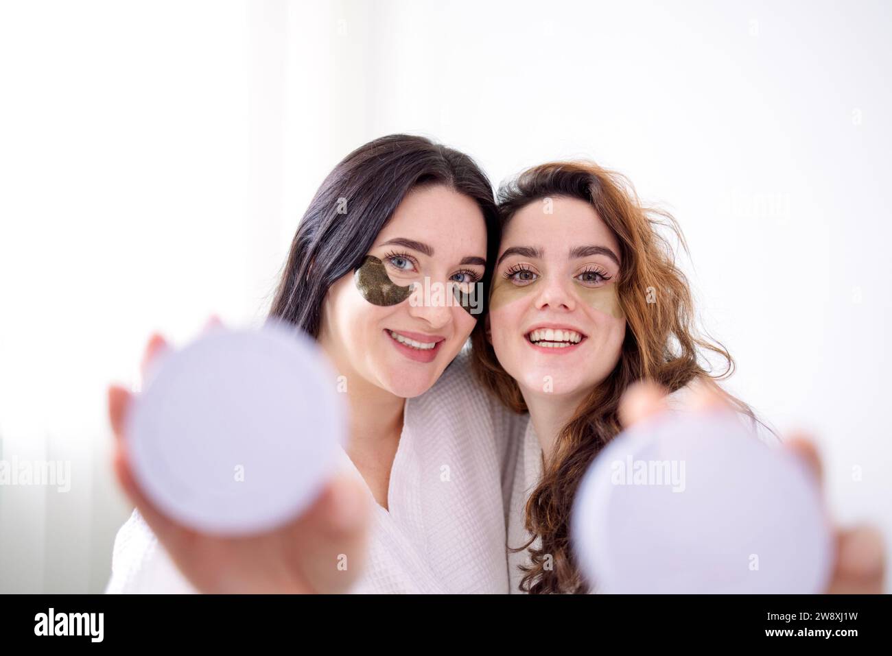 Two young female friends clients of beauty salon in white coats ...