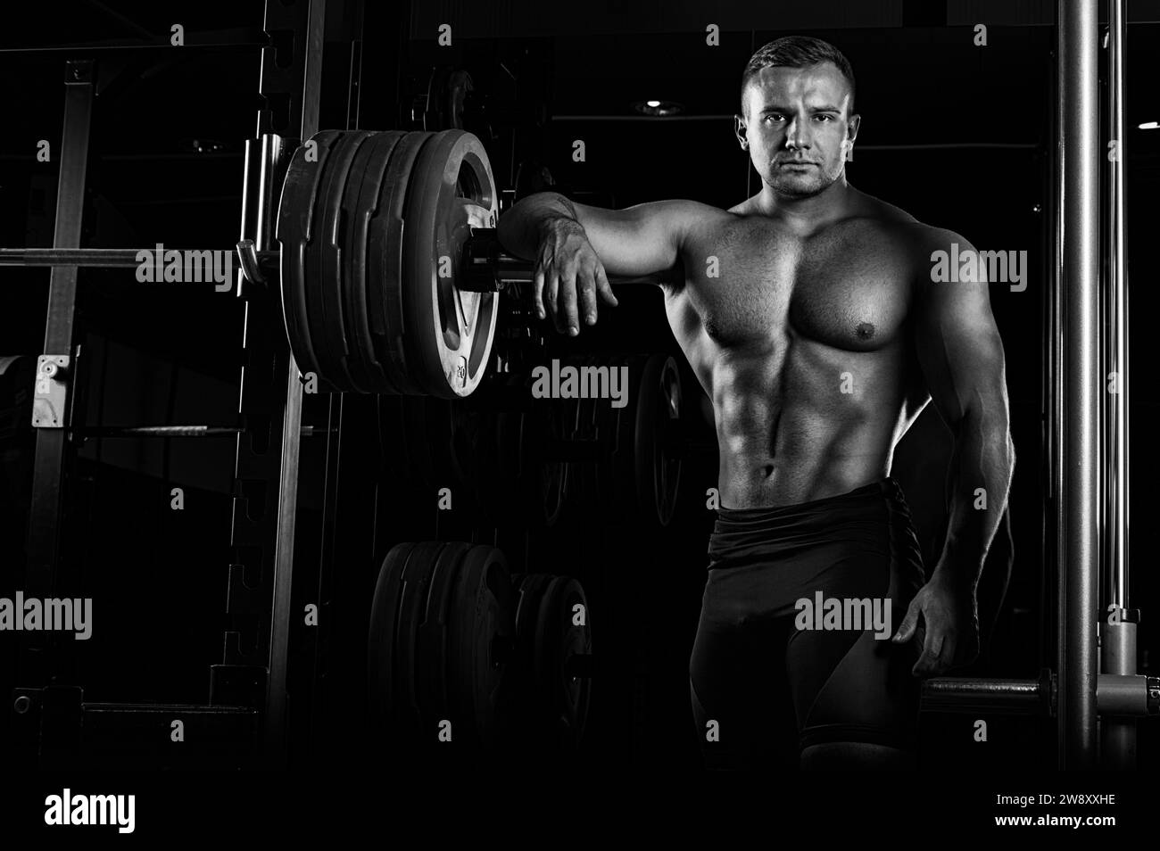 The weightlifter leans his hand on the barbell and looks menacingly ...