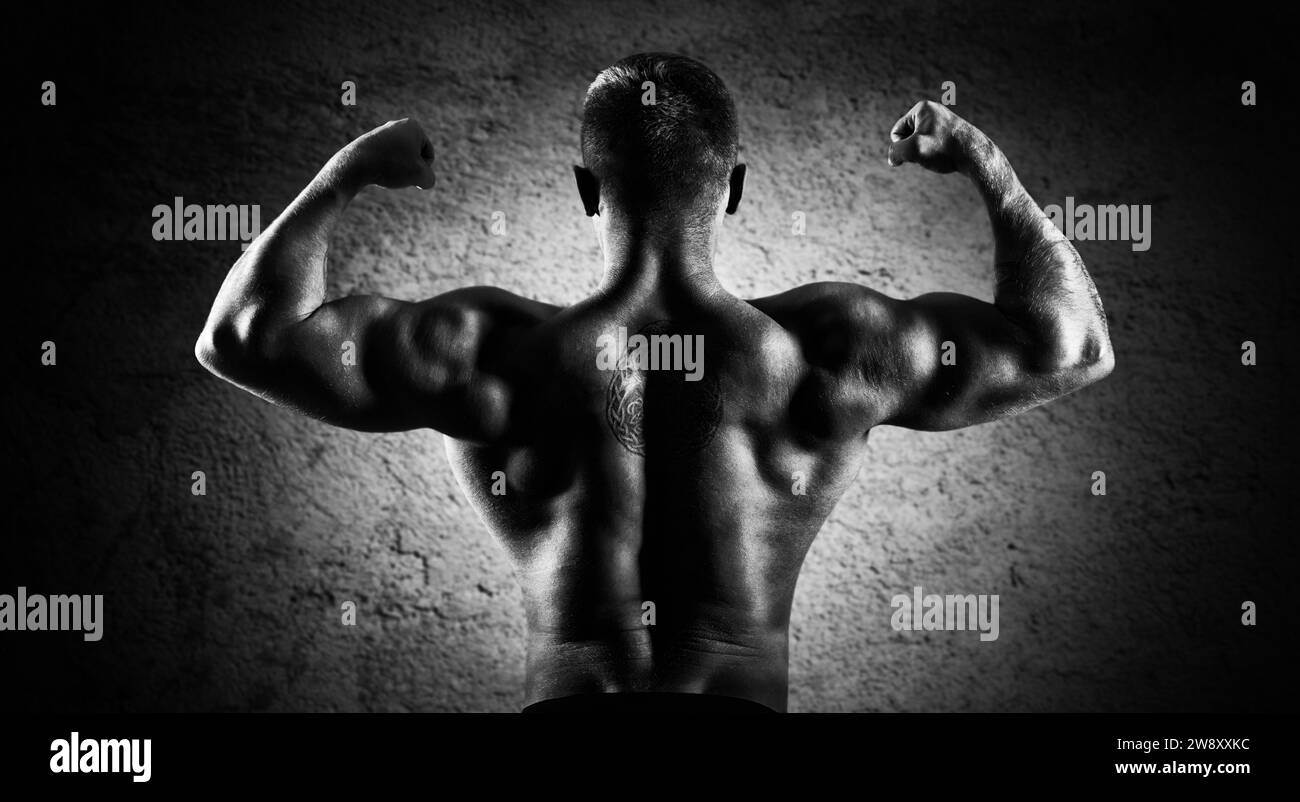 Huge weightlifter is standing with his back to the camera and straining ...