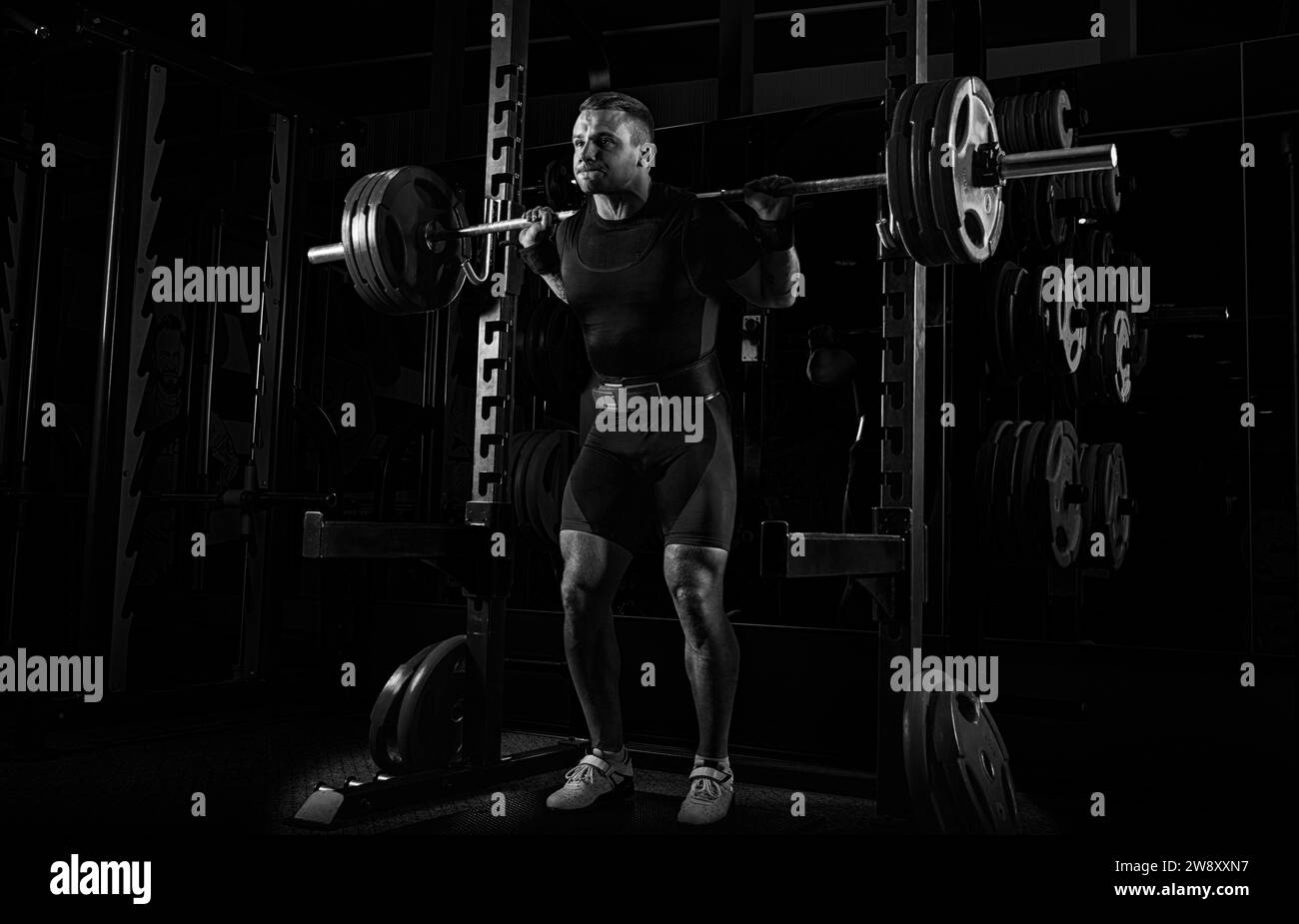 The weightlifter stands with a very heavy barbell on his shoulders. He ...