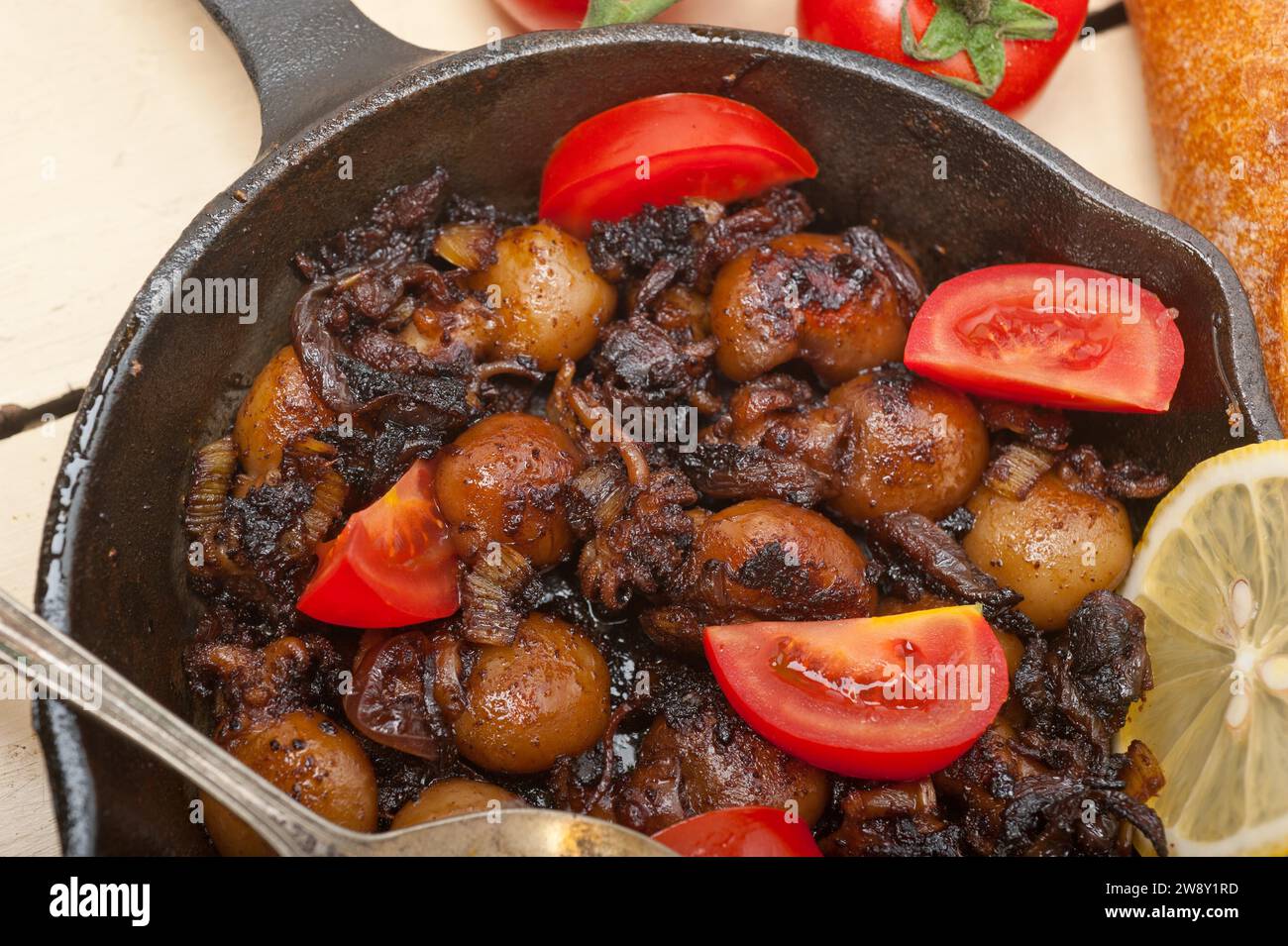 Baby cuttle fish roasted on iron skillet with tomatoes and onions over ...
