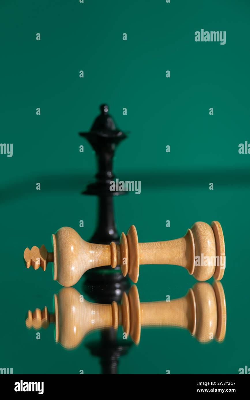 A fallen white queen and a standing black king on a reflective ...