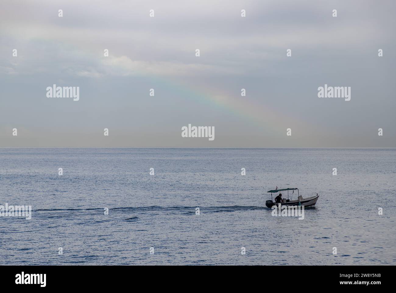 A picture of a fishing boat on the sea with a rainbow in the distance ...