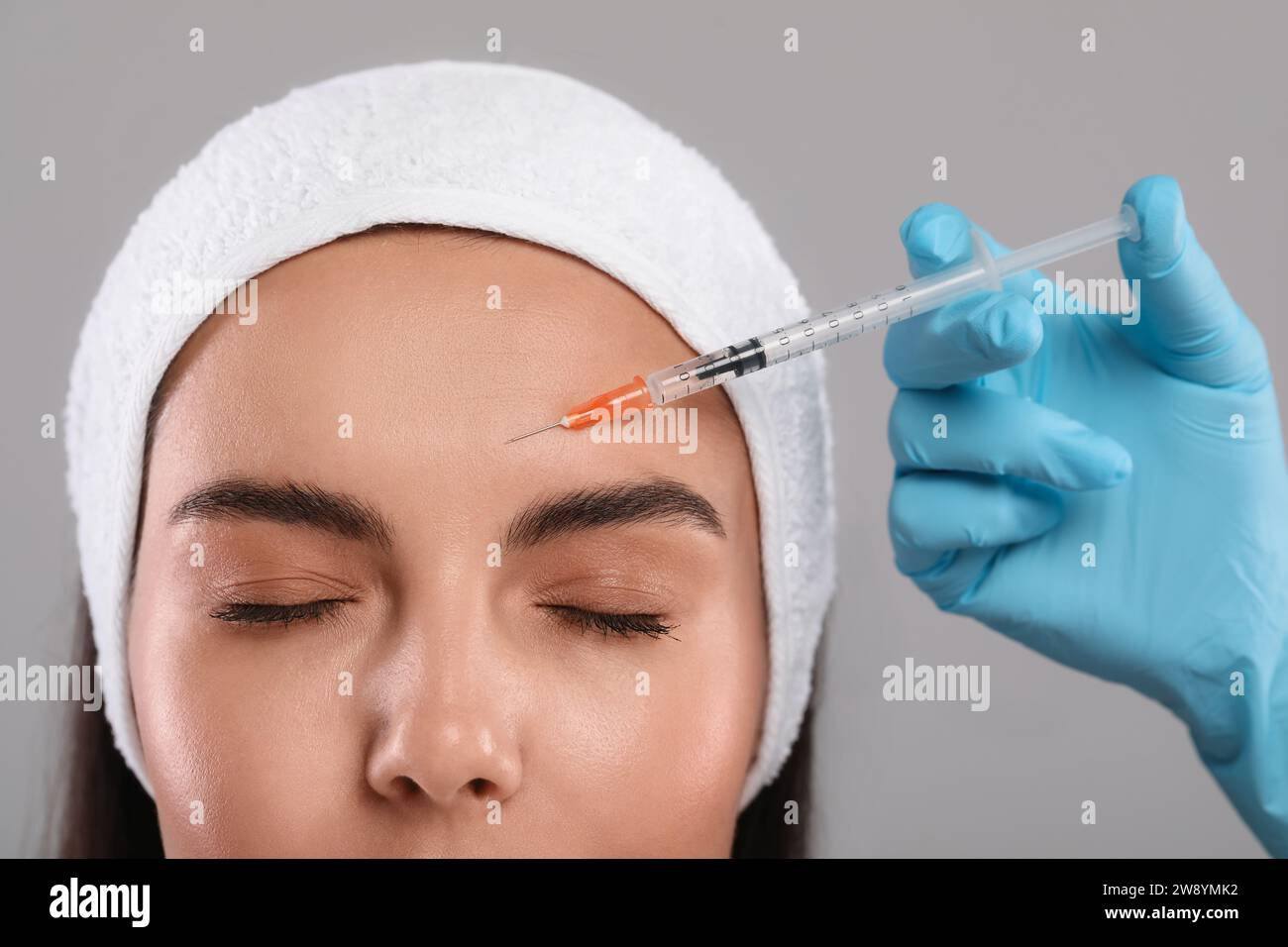 Doctor giving facial injection to young woman on light grey background ...