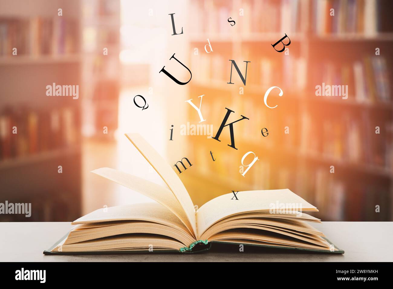 Open book with letters flying out of it in library Stock Photo - Alamy