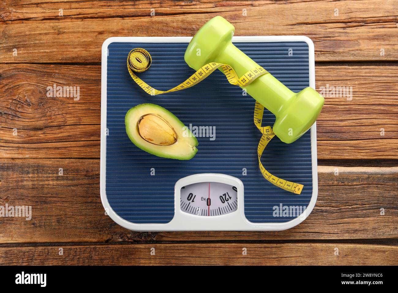 Healthy diet. Scale, avocado, measuring tape and dumbbell on wooden ...