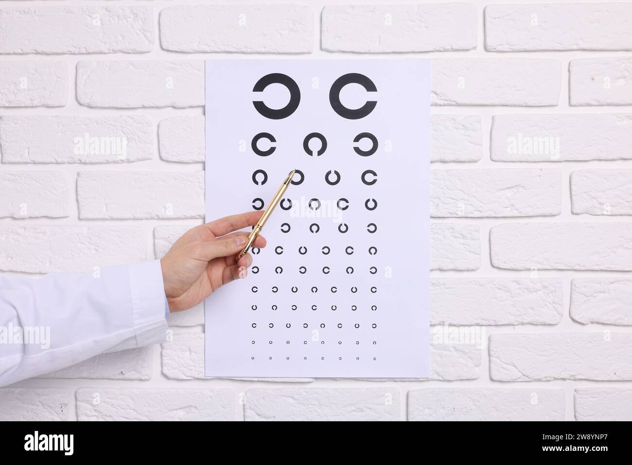 Ophthalmologist pointing at vision test chart on white brick wall ...