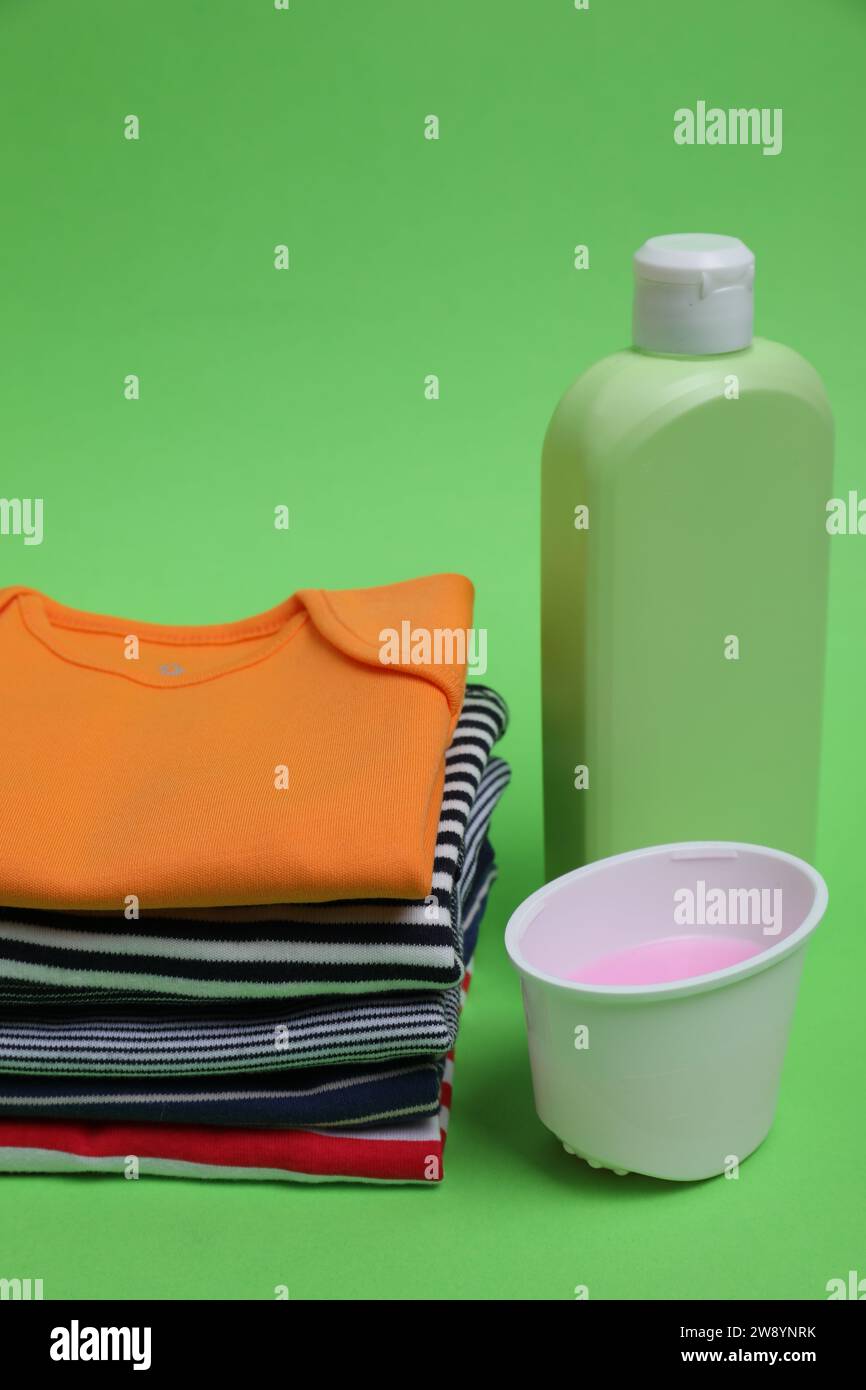Stack of baby clothes and laundry detergents on light green background ...