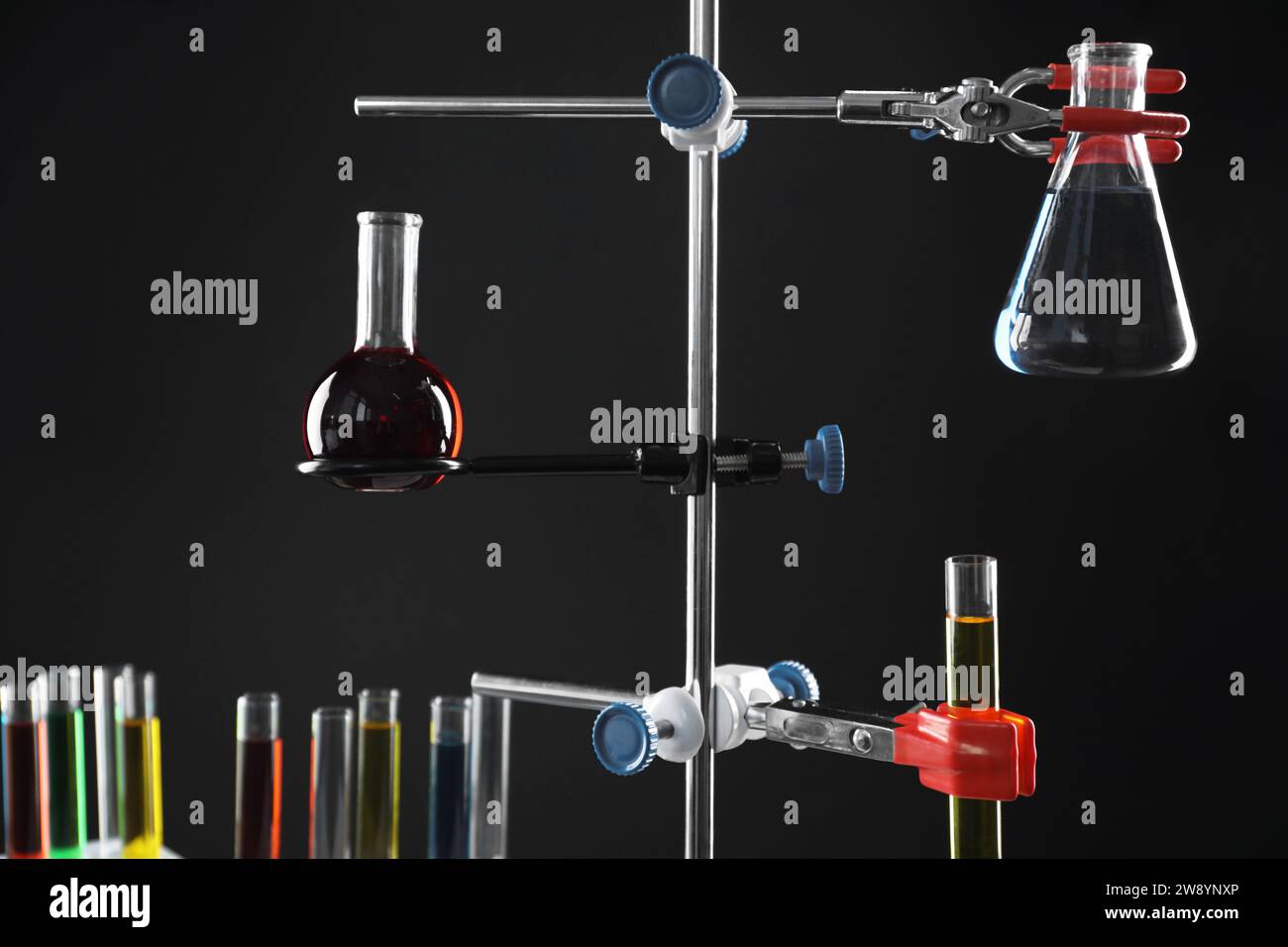 Retort stand and laboratory glassware with liquids on black background ...