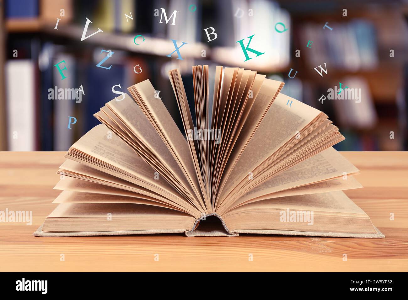 Open book with letters flying out of it in library Stock Photo - Alamy