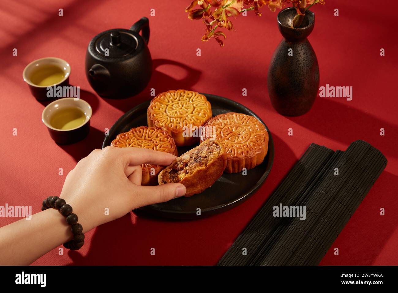 Hand of female holding halve of mooncake from dish of mooncakes. Black ...