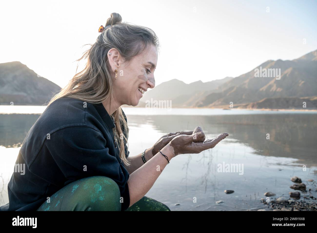 Woman putting mud on hands and face while enjoying outdoors in nature ...