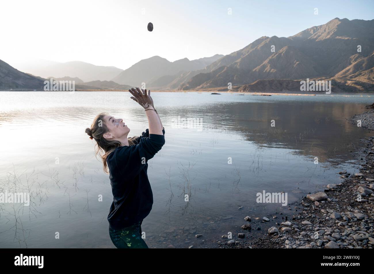 Woman putting mud on hands and face while enjoying outdoors in nature ...