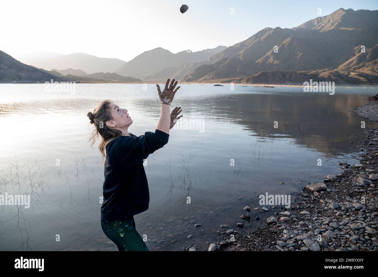 Woman putting mud on hands and face while enjoying outdoors in nature ...