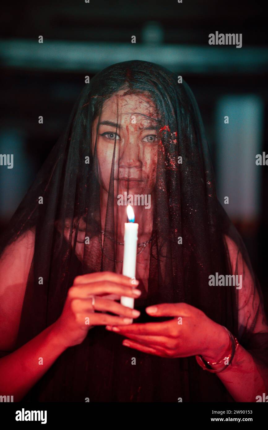 an Asian woman with a transparent veil covered in blood holds a candle ...