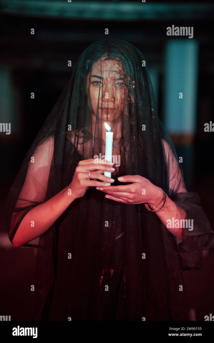 an Asian woman with a transparent veil covered in blood holds a candle ...
