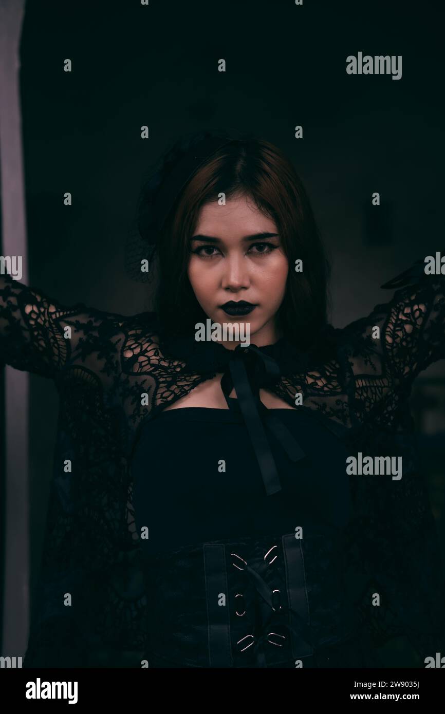 a goth Asian woman dresses up with black make up and wears black ...
