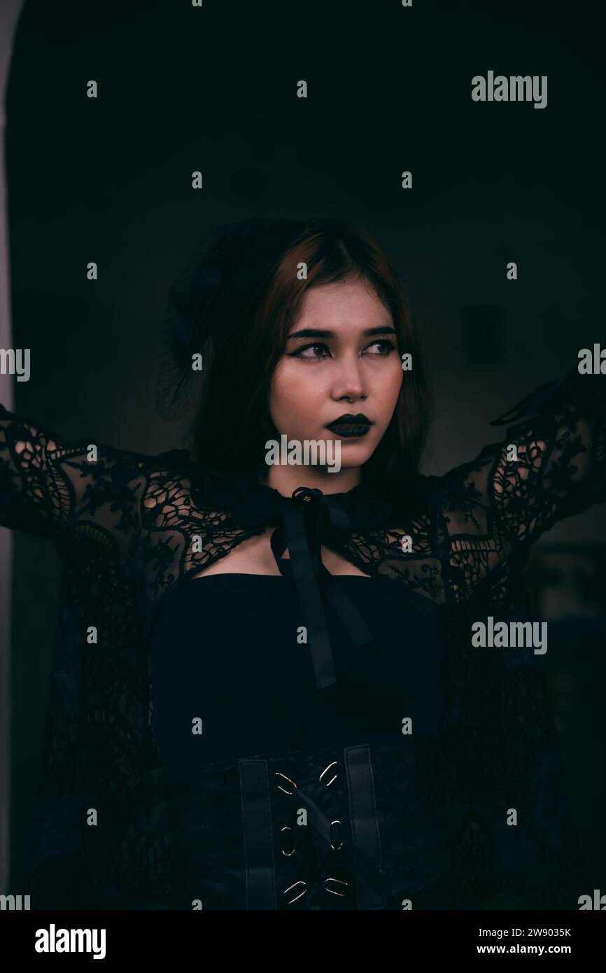 a goth Asian woman dresses up with black make up and wears black ...