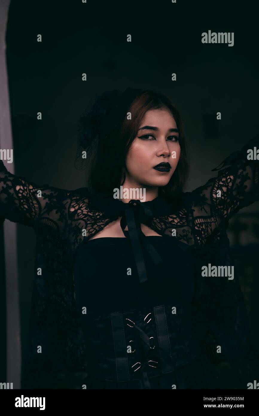 a goth Asian woman dresses up with black make up and wears black ...