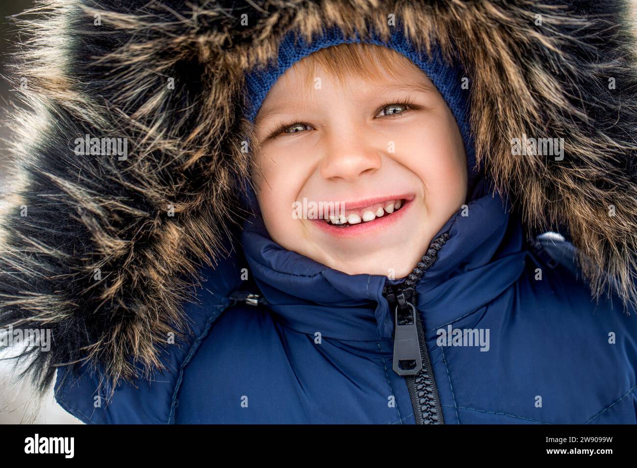 Boy wearing a fur hooded winter coat. Close up portrait of cute happy smiling child on a cold ...