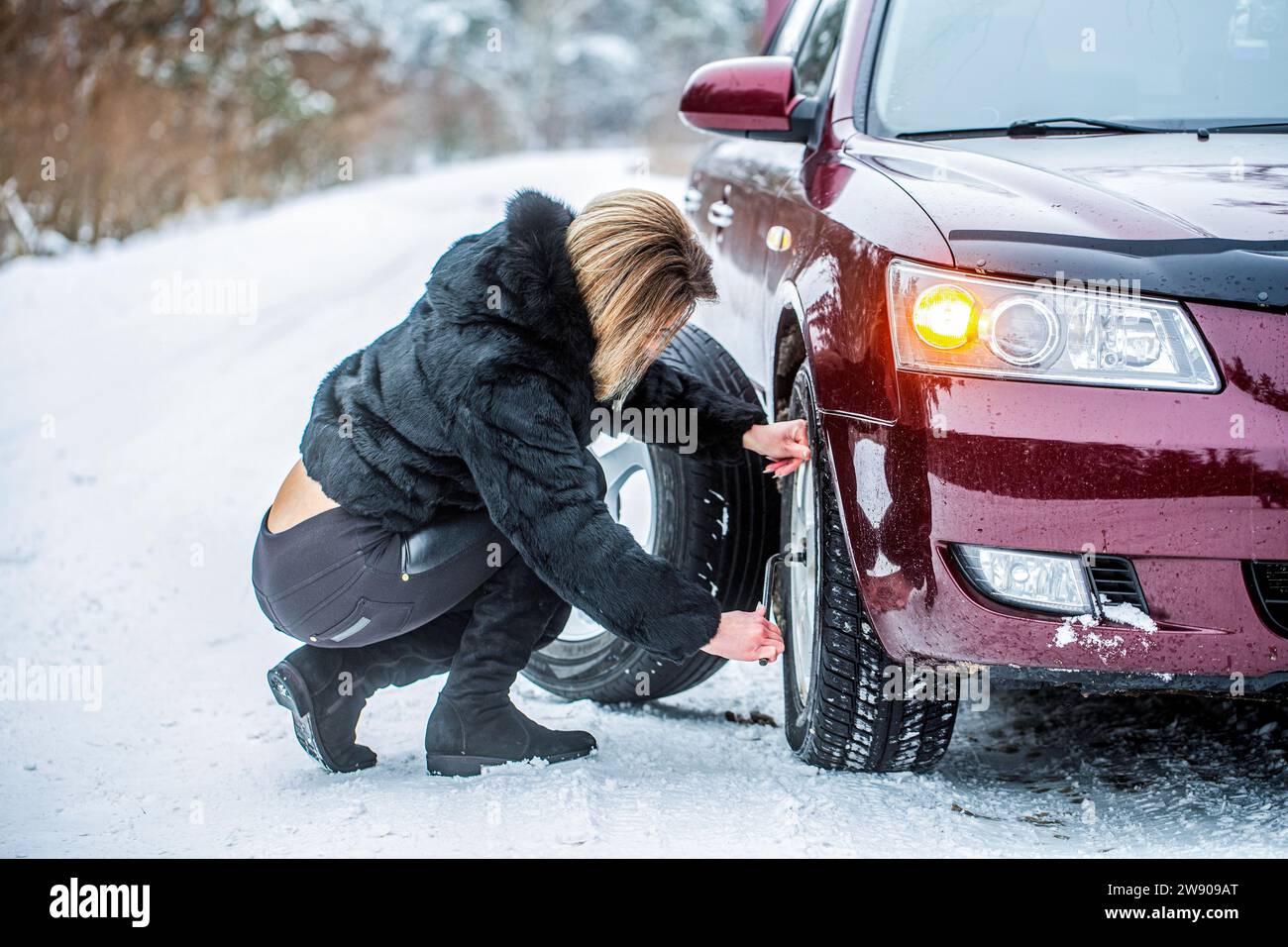 Woman changing the punctured tyre on his car in winter. Pretty girl ...
