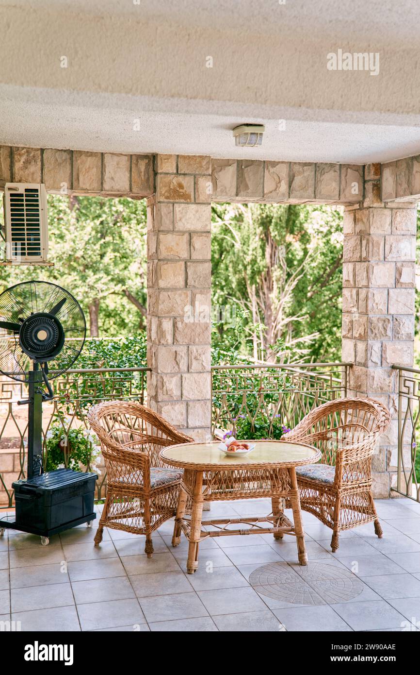 Wicker chairs stand around a table on the terrace of a stone house near ...