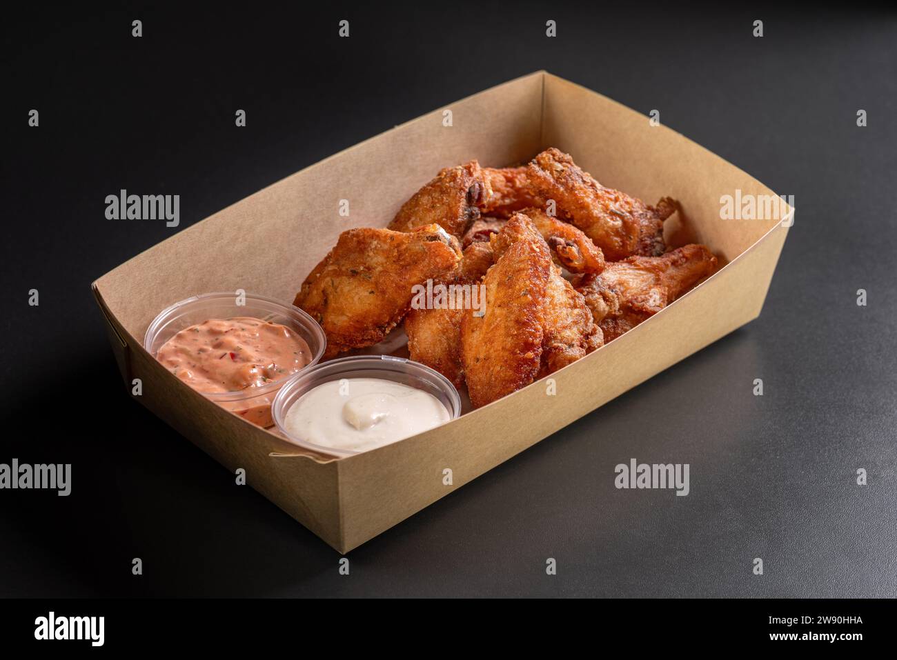 Fried chicken wings in a paper box on a dark background. Snacks in a ...