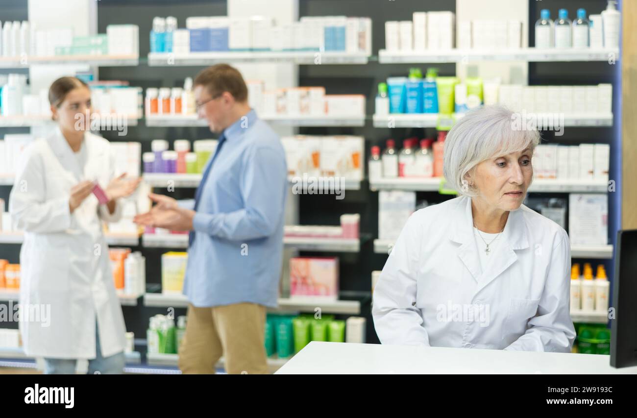 Old female pharmacist looking at display of computer in chemist's shop ...