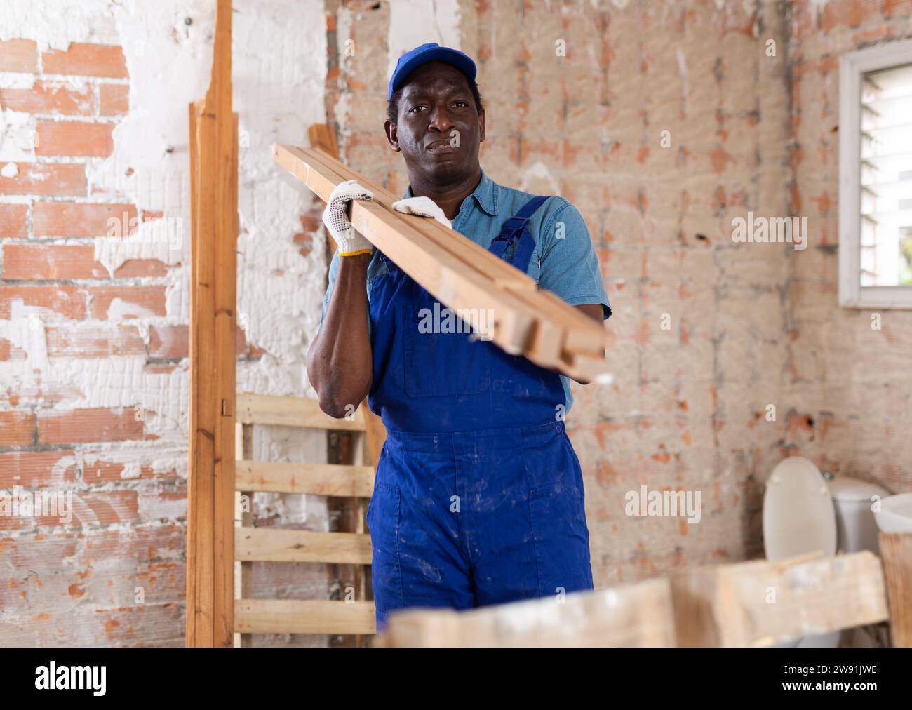 Man builder carrying wooden planks in construction site Stock Photo - Alamy