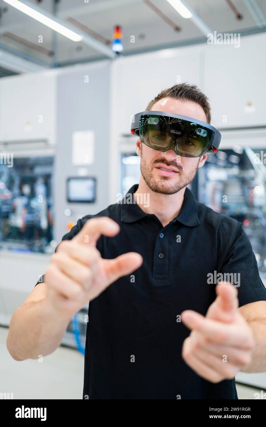 Technician wearing augmented reality glasses and gesturing in a factory ...
