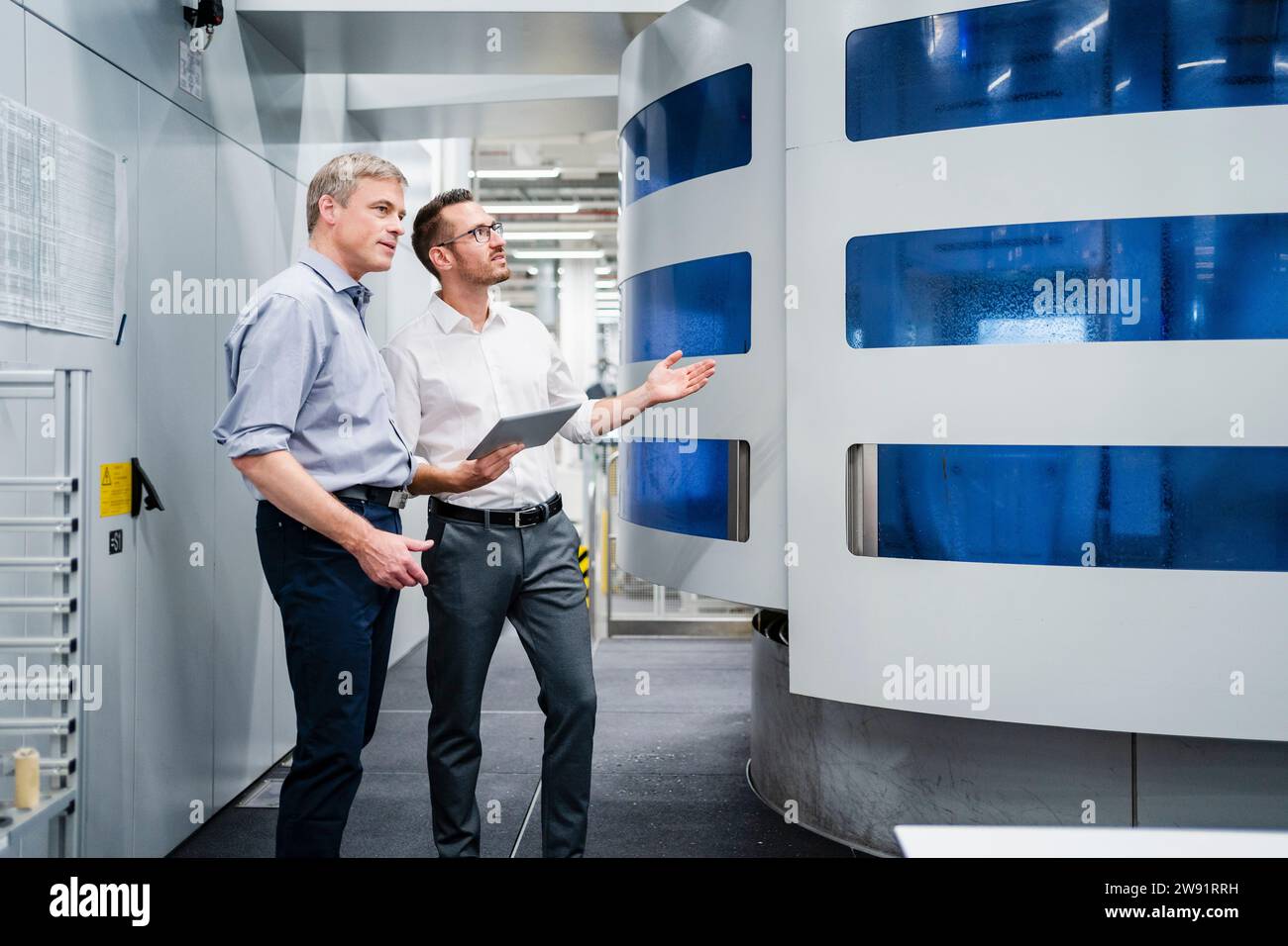Two businessmen with digital tablet looking at machine in a factory ...