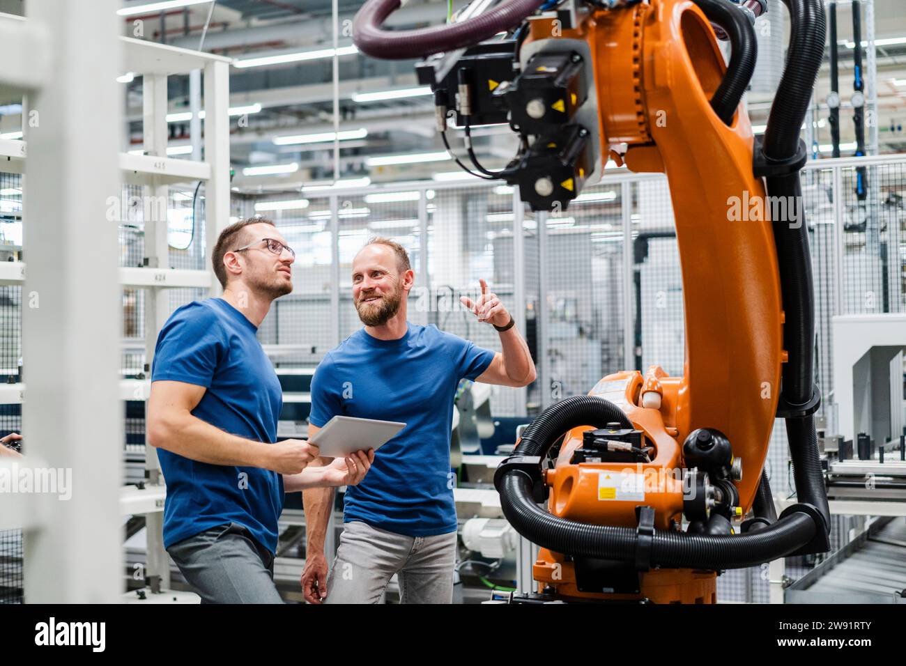 Two technicians with digital tablet examining industrial robot in a ...