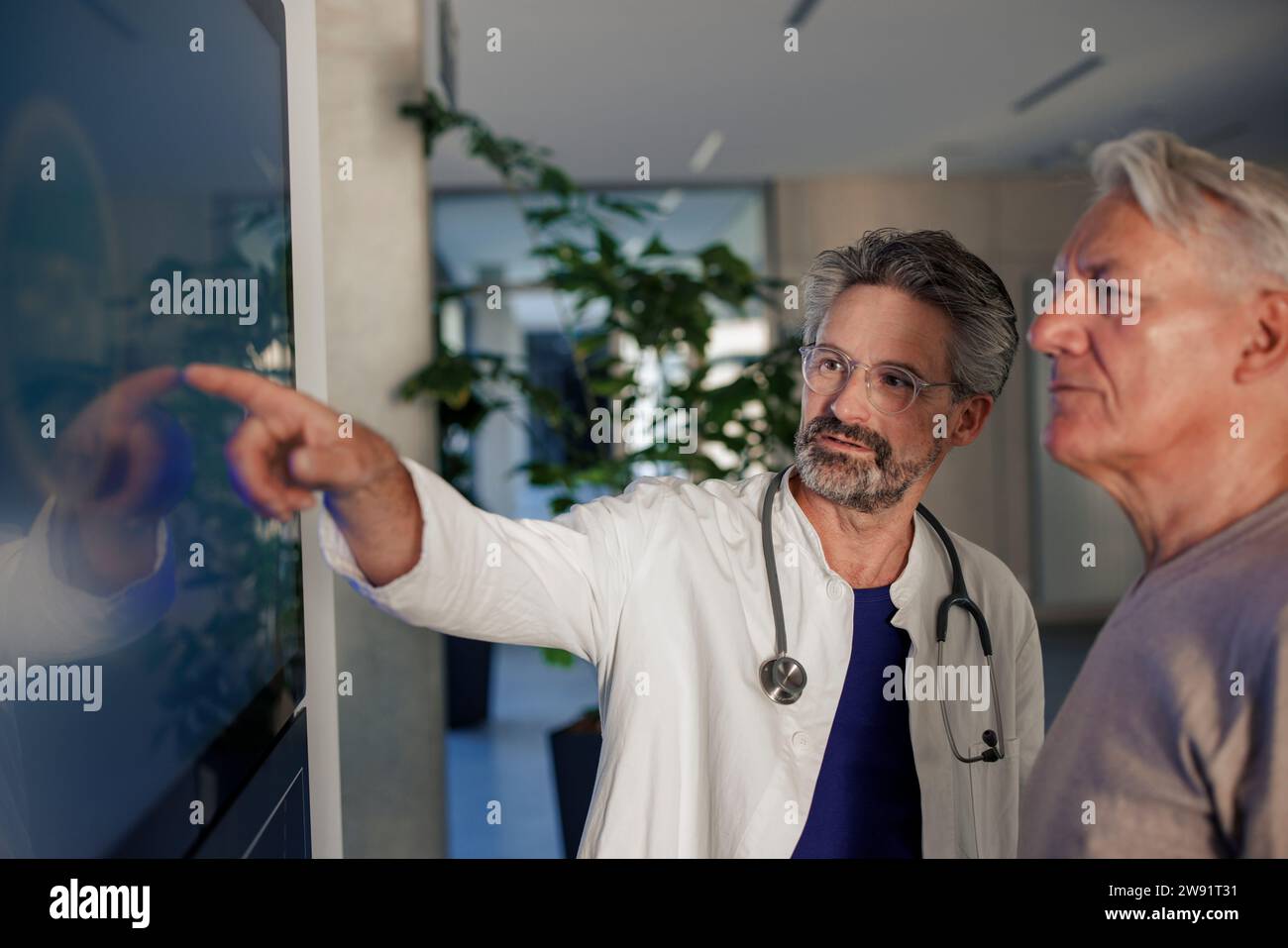 Senior doctor explaining man over device screen in hospital Stock Photo ...