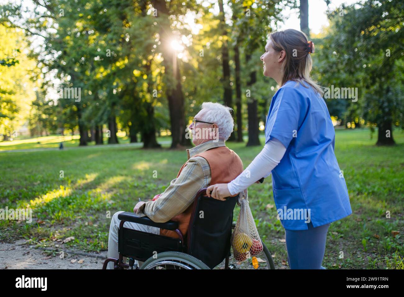 Healthcare worker walking with senior man sitting in wheelchair near ...
