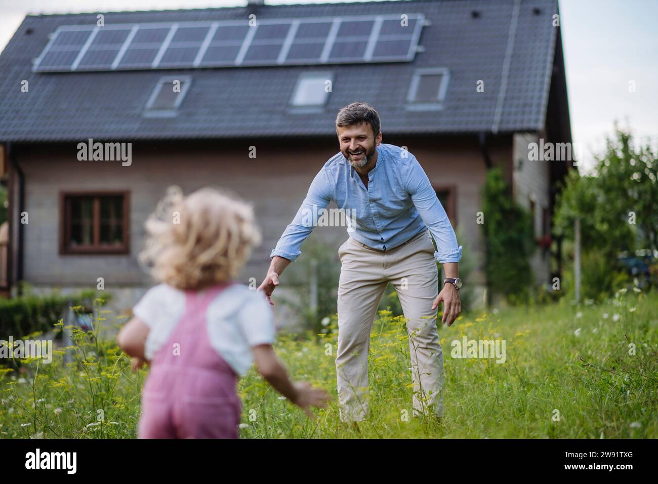 Lttle daughter running to father in front their family house with solar ...