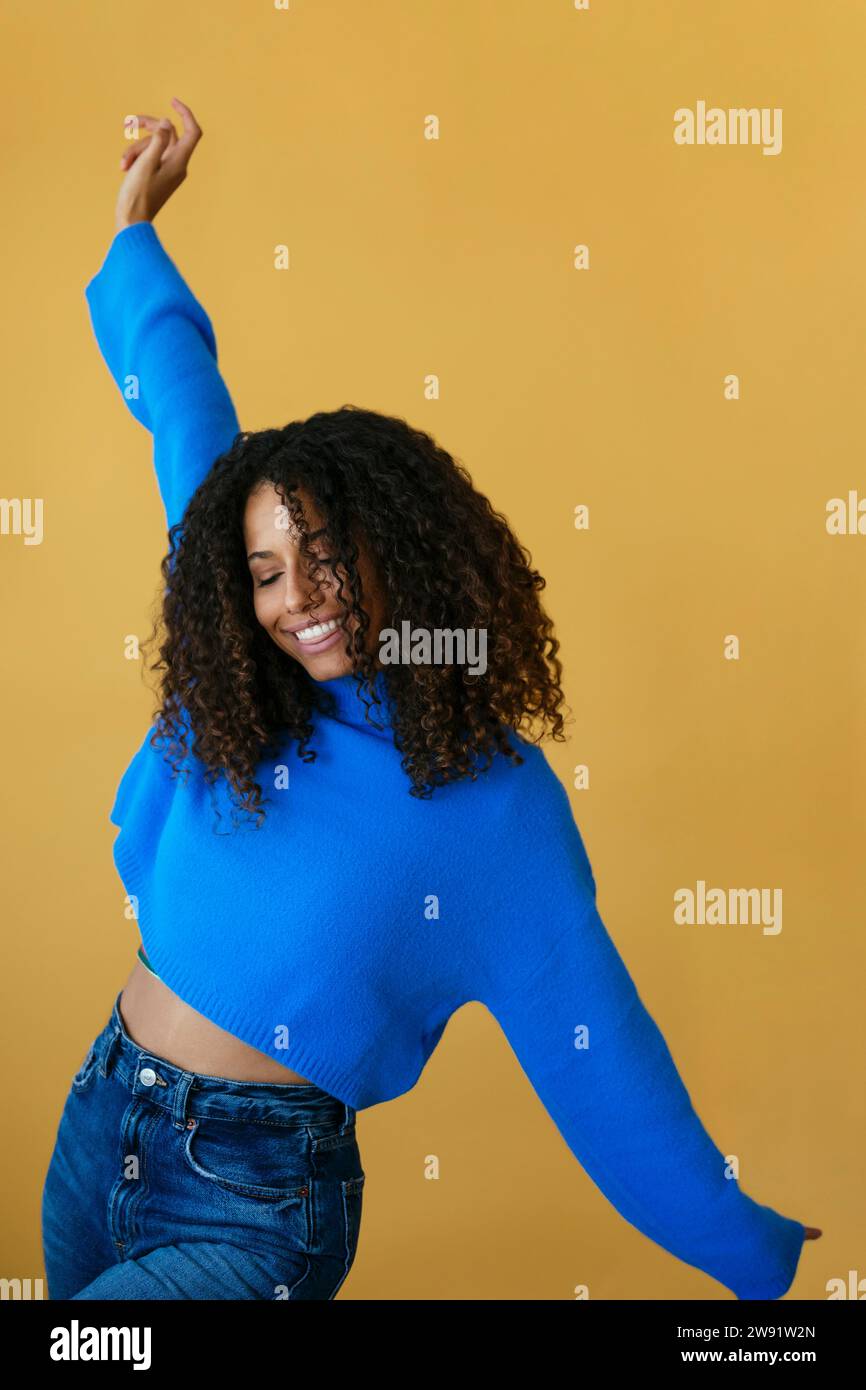 Smiling woman wearing blue sweater and dancing against yellow ...
