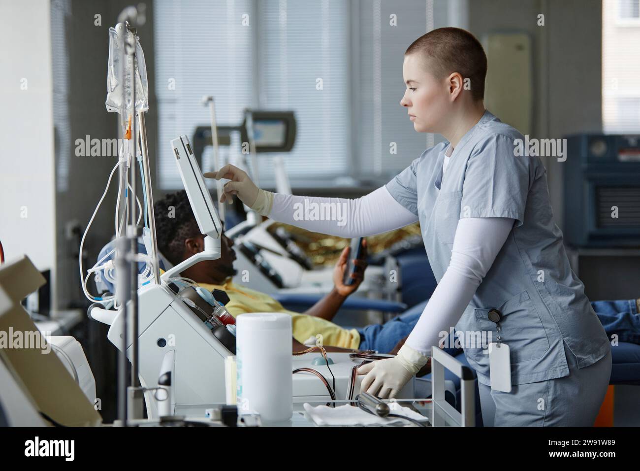 Young healthcare worker operating equipment at blood donation center ...