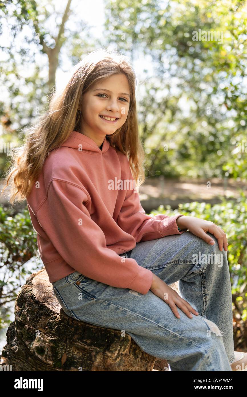 Happy girl sitting on log in park Stock Photo - Alamy