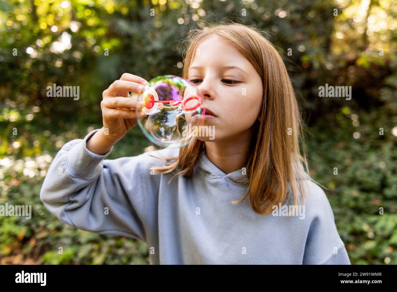 Girl blowing bubble with wand in park Stock Photo - Alamy