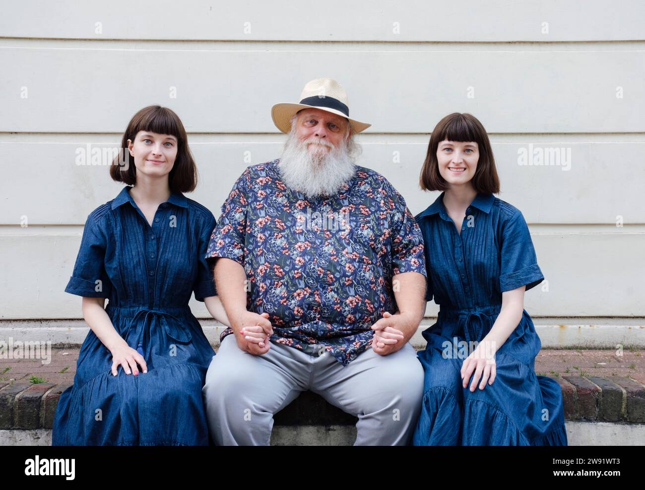 Father holding hands with daughters sitting in front of wall Stock ...