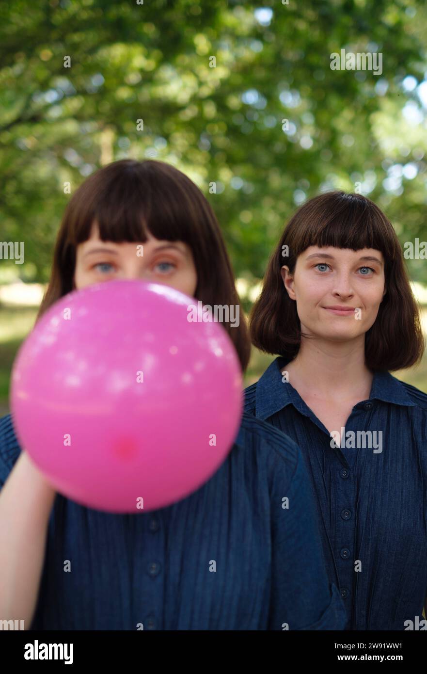 Smiling Young Woman With Sister Blowing Pink Balloon In Park Stock