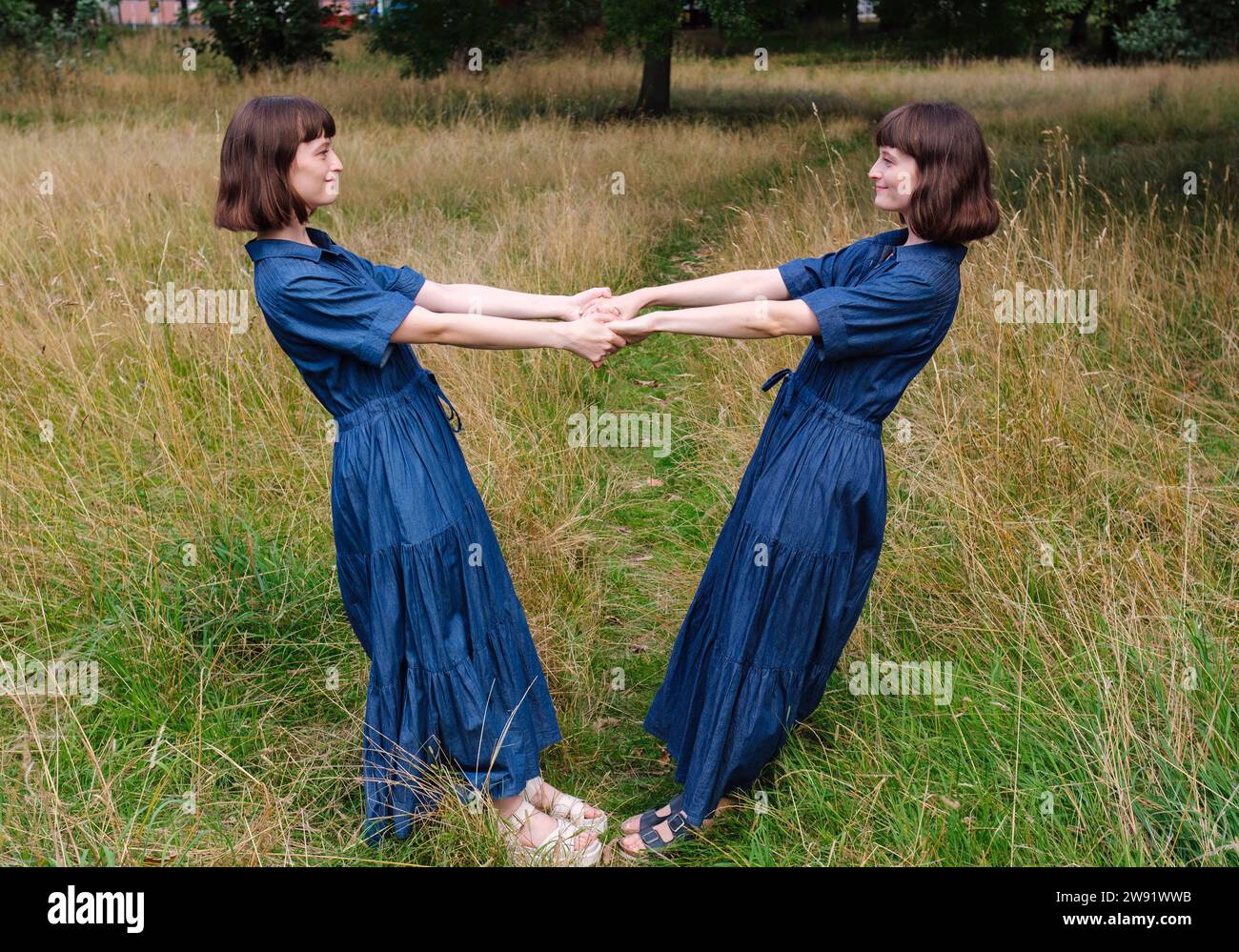 Playful twin sisters holding hands and standing in park Stock Photo - Alamy