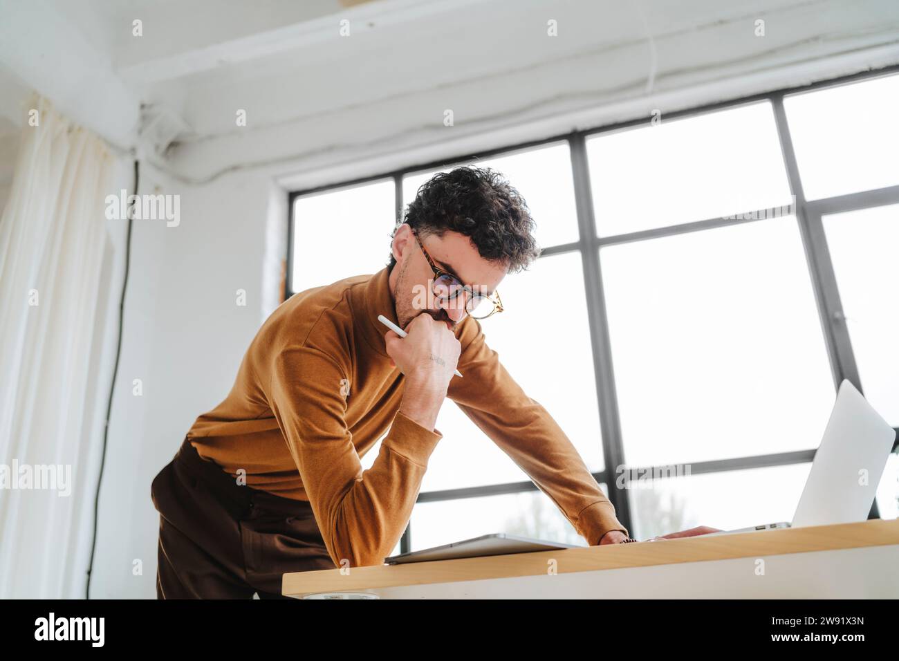 Focused graphic designer leaning on desk at office Stock Photo - Alamy