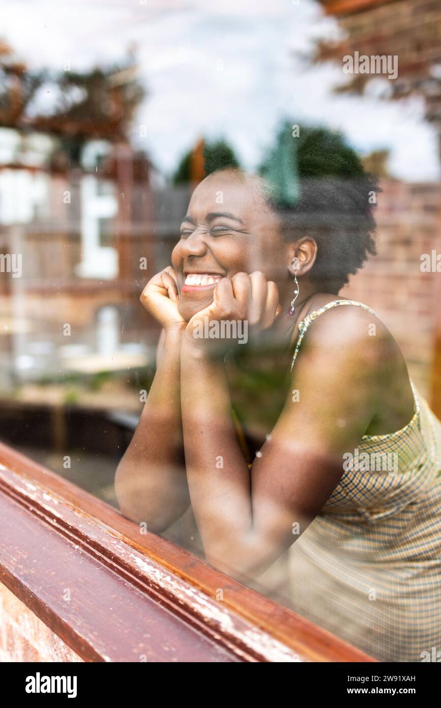 Happy young woman leaning on elbow seen through window Stock Photo - Alamy