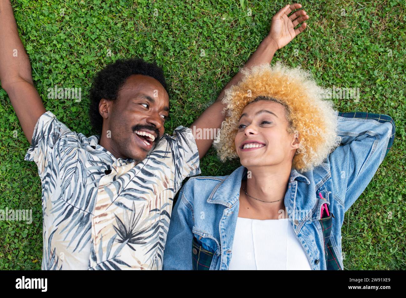 Happy man with arms raised lying next to transgender woman on grass at ...