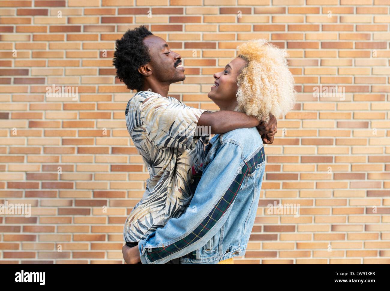 Boyfriend with arm around transgender woman in front of brick wall ...